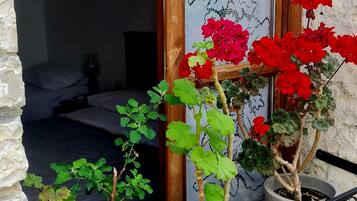 Uma varanda com plantas em vasos, um corrimão de madeira e vista para um quarto com cama e janela.