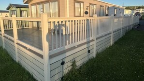 Uma casa móvel com um deck cercado, uma garagem e um pequeno alpendre.