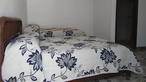 Uma cama com colcha florida num quarto com chão de azulejos e uma porta.