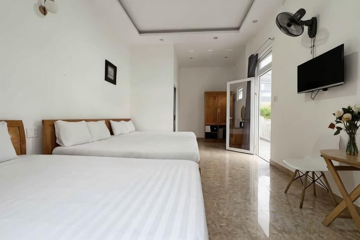 Quarto de hotel com duas camas, televisão, escrivaninha e área de refeições.