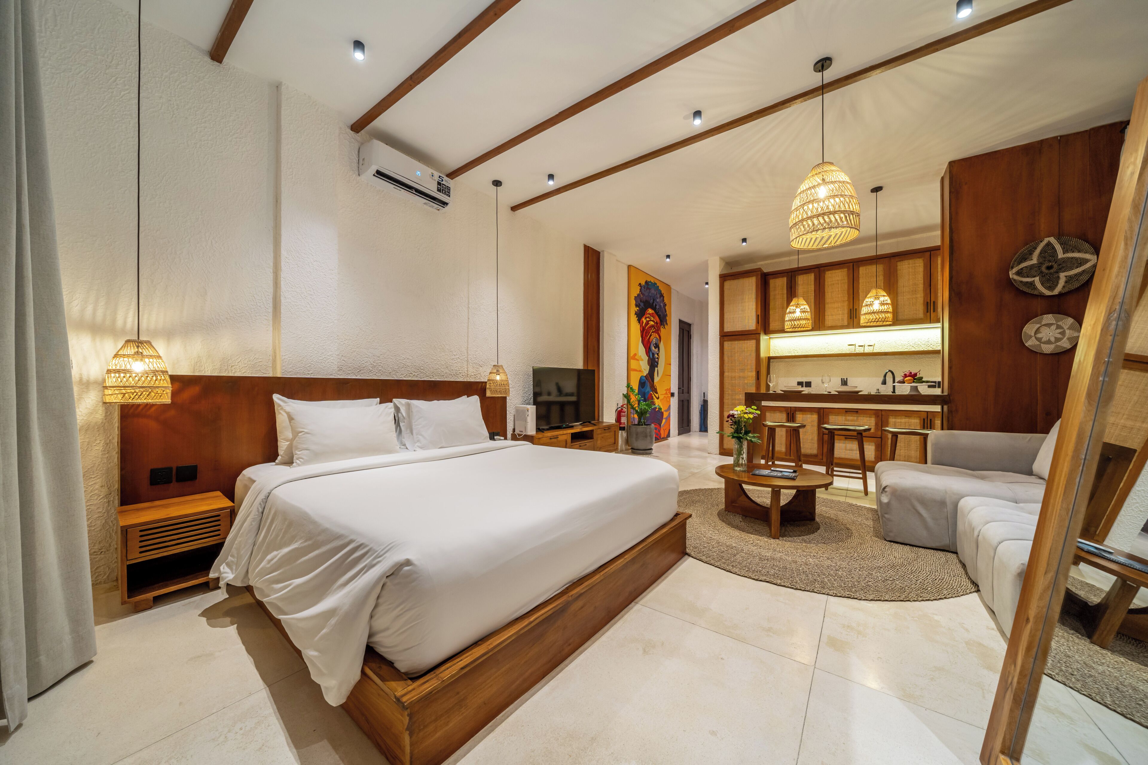 Quarto de hotel com uma cama grande, uma mesa, um sofá e uma cozinha compacta.