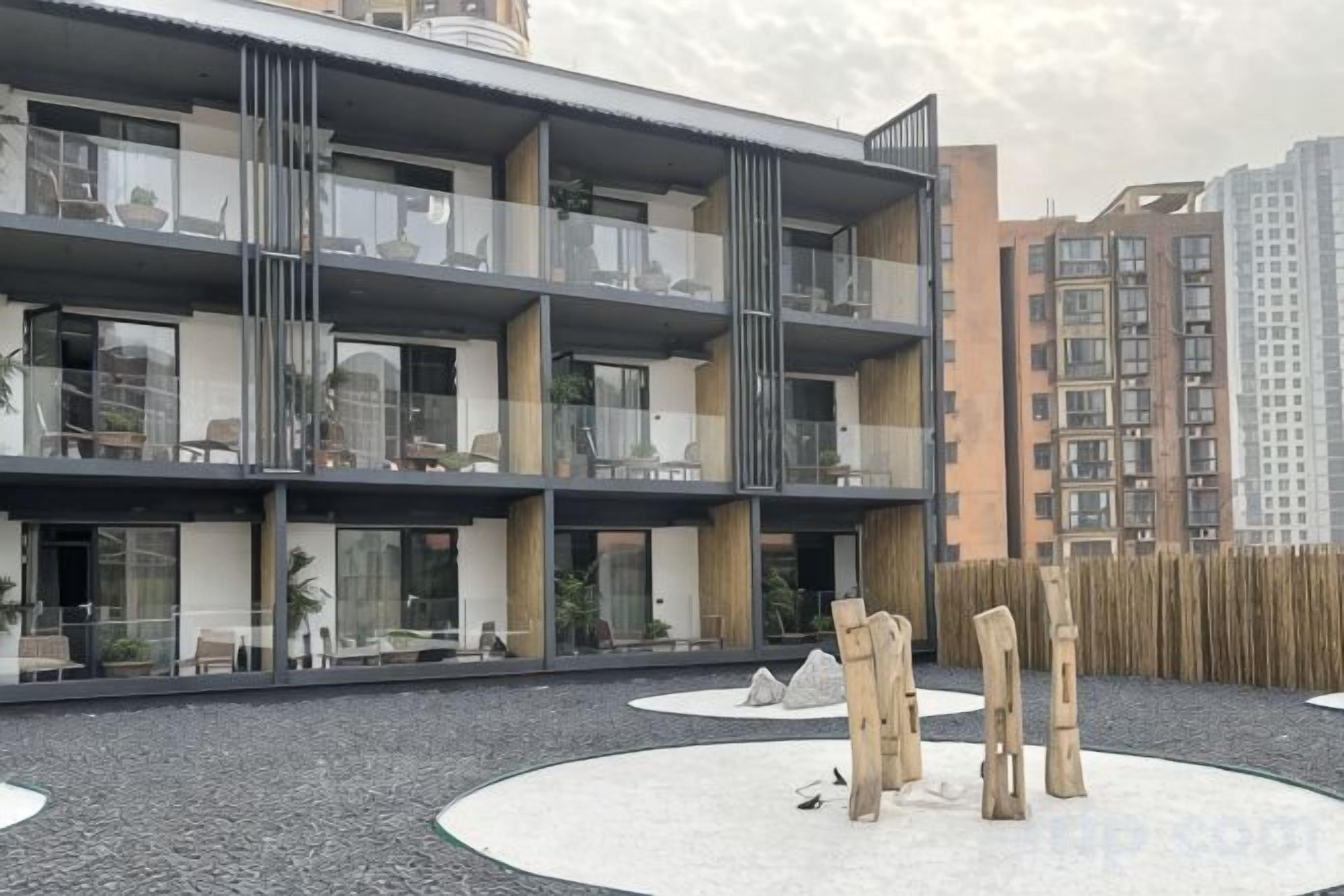 Hotel com vários andares, varandas, um pátio com escultura de madeira e vista para edifícios próximos.