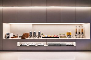 Um balcão de café da manhã moderno com máquinas de café, uma variedade de frutas e um dispensador de café.