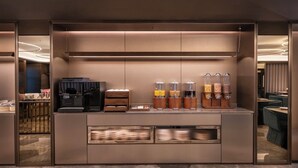 Quarto de hotel moderno com cozinha compacta, máquina de café e bancada para café da manhã com dosadores.