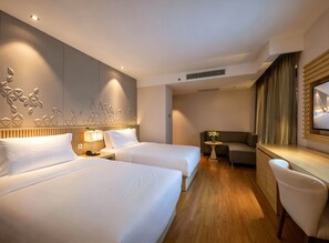 Quarto de hotel com duas camas, um sofá, uma mesinha e uma televisão.