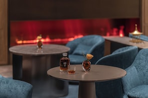 Uma área de estar moderna com mesas redondas, cadeiras estofadas em azul e um vaso decorativo com uma única rosa.
