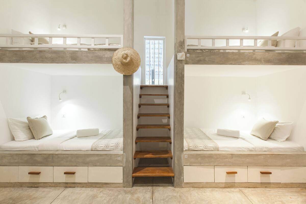 Quarto com beliches, uma escada central e uma janela com vista.