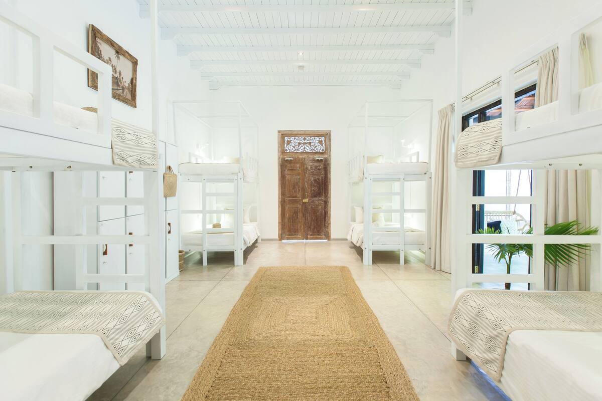 Quarto com beliches, um tapete grande e uma porta de madeira.