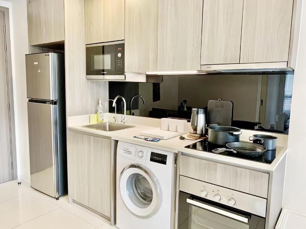 Cozinha compacta com geladeira de aço inoxidável, máquina de lavar embutida, micro-ondas e fogão.