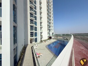 Um edifício moderno com área de piscina no terraço, incluindo espreguiçadeiras e guarda-corpo de vidro.