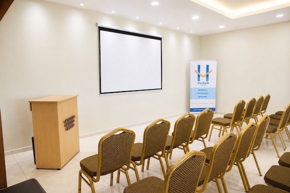 Uma sala de conferências com um púlpito, uma tela de projeção e fileiras de cadeiras de vime.