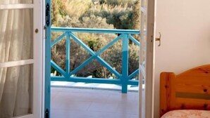 Quarto com vista para uma encosta, varanda com guarda-corpo azul e cama com colcha florida.