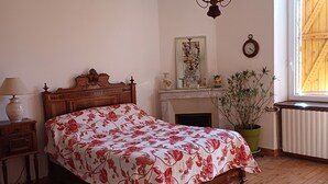 Quarto com cama de madeira, mesa de cabeceira, espelho, relógio, janela com vista e planta em vaso.