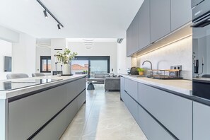 Uma cozinha moderna com ilha central, eletrodomésticos embutidos e área de refeições com sofá e mesa de centro.