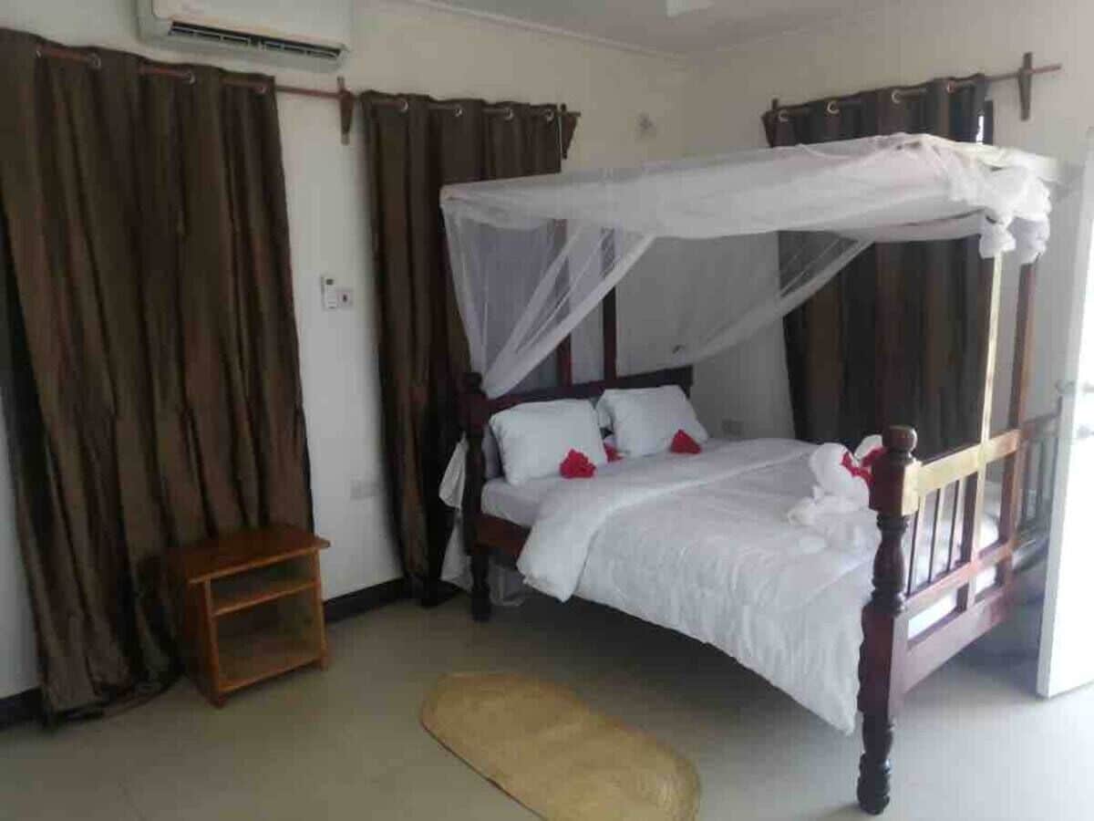 Uma cama de solteiro com dossel, uma mesa de cabeceira e um banco.