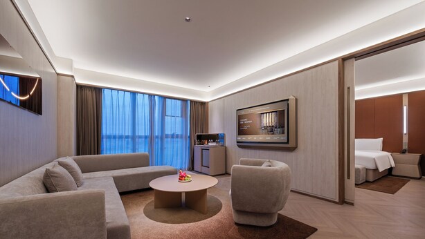 Quarto de hotel moderno com sofá, poltrona, mesa de centro e televisão na parede.