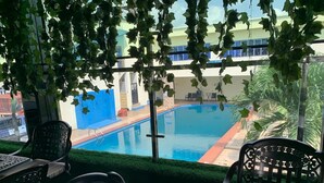 Área interna de piscina com vista para um edifício, rodeada por vegetação e mobiliada com assentos externos.
