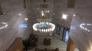 Um hall amplo com um lustre imponente, paredes de mármore e uma área de estar com mobiliário de madeira.