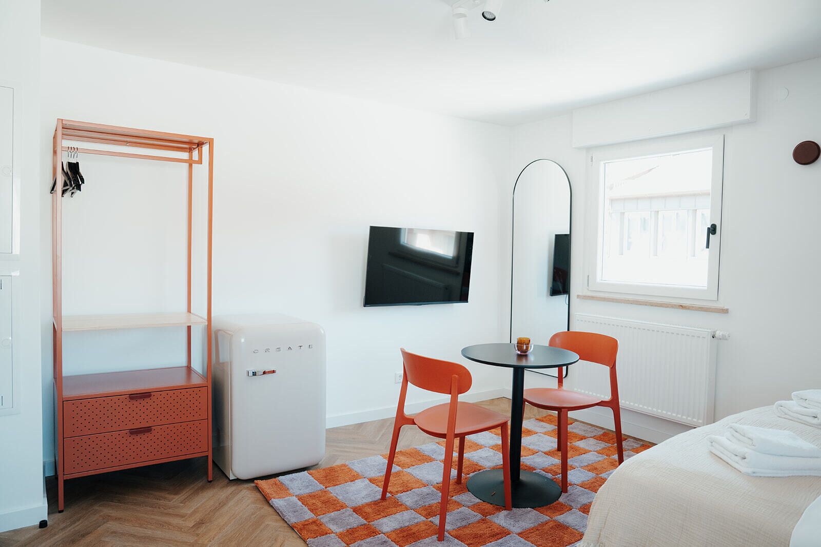 Quarto de hotel com cama, uma mesinha com duas cadeiras, televisão e guarda-roupa.