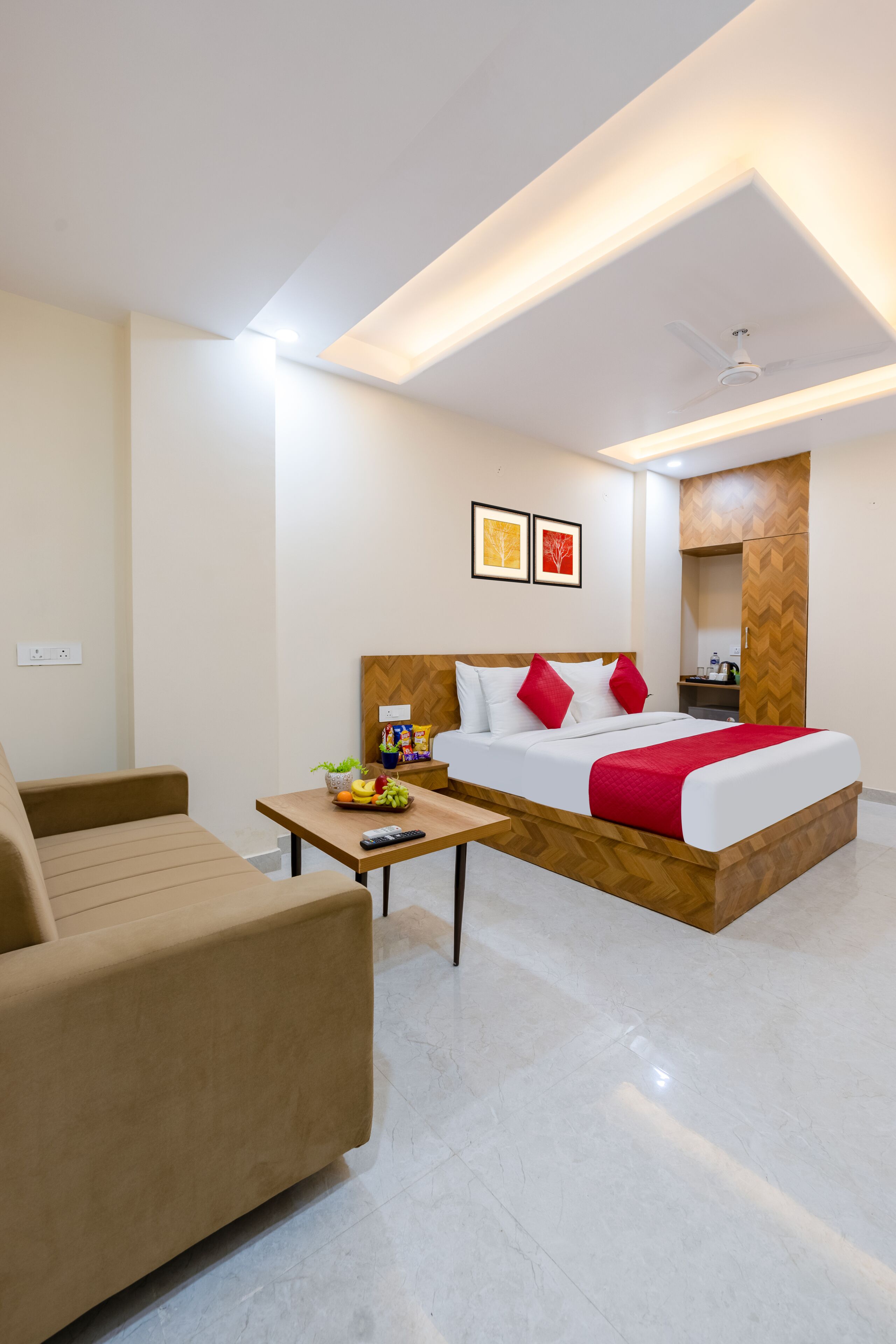 Quarto de hotel com uma cama, um sofá, uma mesinha com petiscos e um ventilador de teto.