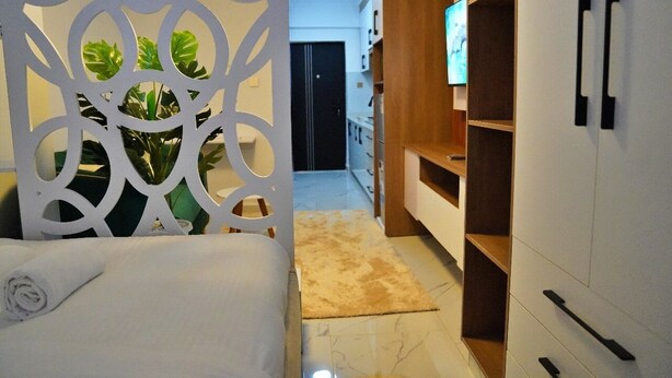 Quarto de hotel com cama, televisão, guarda-roupa de madeira e um divisória decorativa com plantas.