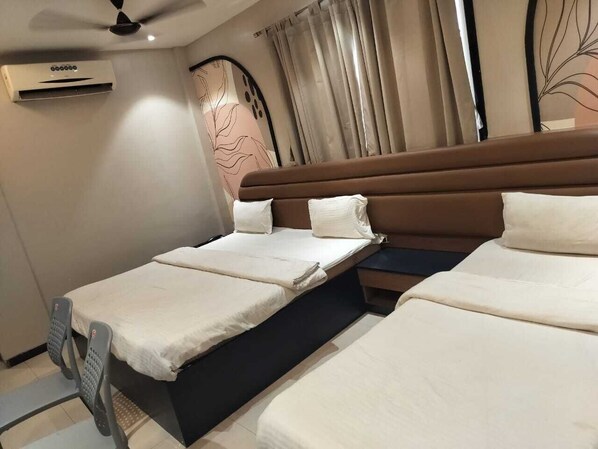 Quarto de hotel com duas camas, um ventilador de teto, aparelho de ar condicionado e uma janela com cortinas.
