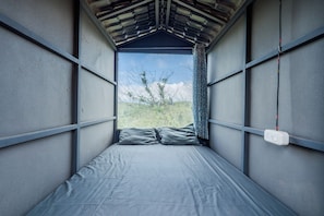 Um quarto pequeno e fechado, com uma cama, uma janela e vista para o exterior.