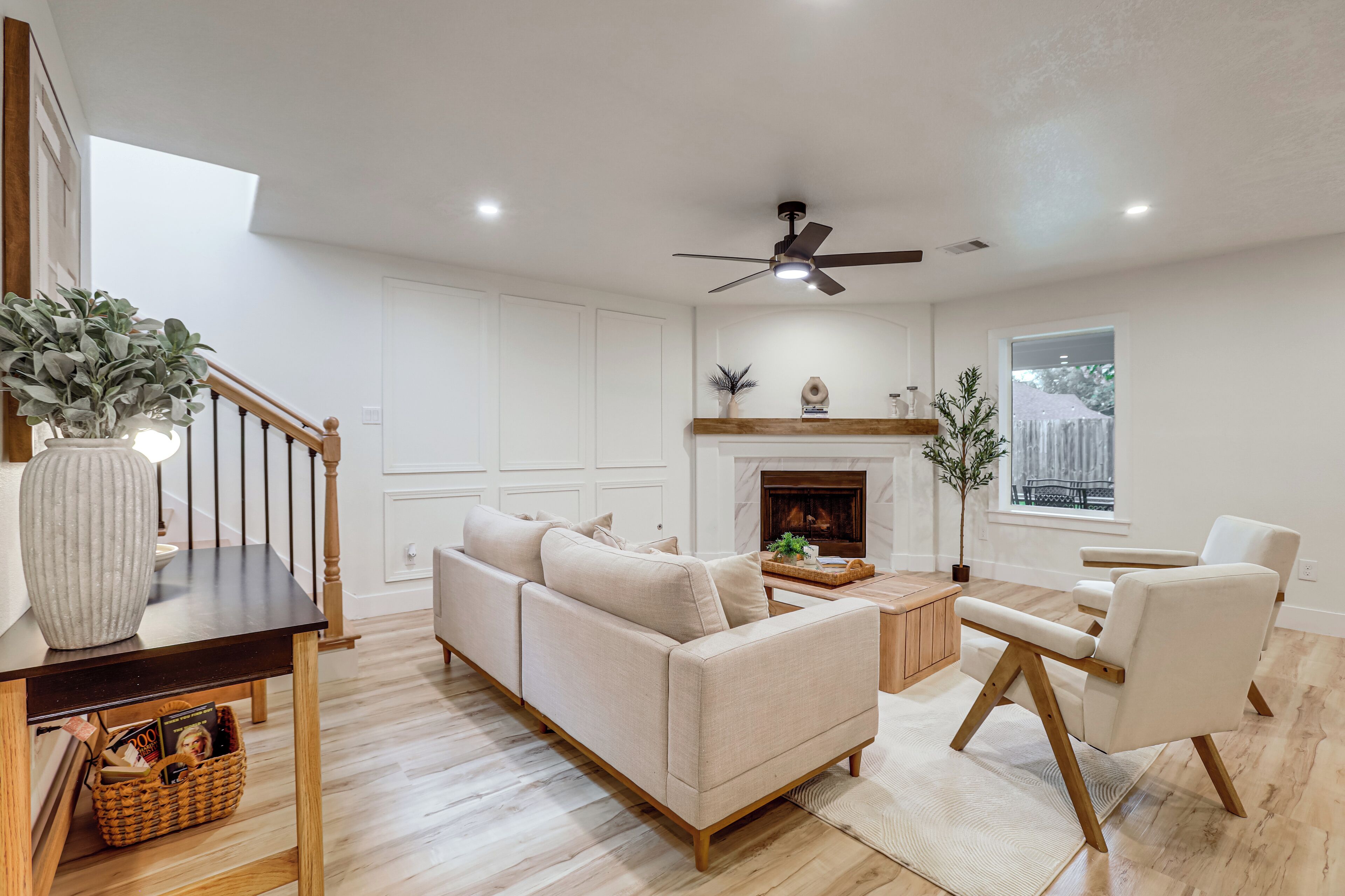 Uma sala de estar moderna com sofá, poltronas, lareira e ventilador de teto.