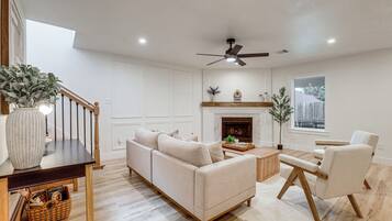 Uma sala de estar moderna com sofá, poltronas, lareira e ventilador de teto.