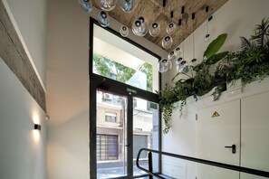 Um interior moderno com entrada por porta de vidro, escada e teto com luminárias esféricas pendentes.