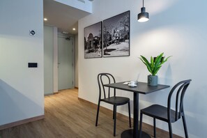 Uma sala de jantar moderna com uma mesa, cadeiras, uma planta em vaso e duas fotografias emolduradas a preto na parede.