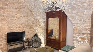 Um quarto com paredes de pedra, uma televisão, um armário de madeira e um sofá.