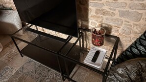 Sala de estar com televisão de tela plana sobre uma mesa de vidro, parede de pedra e sofá estampado.