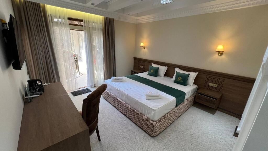 Quarto de hotel com cama, mesas de cabeceira, escrivaninha, cadeira e televisão.