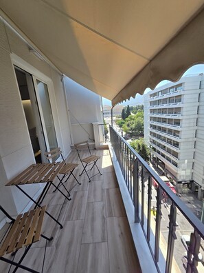 Uma varanda com mesa e cadeiras, vista para um horizonte urbano e um edifício com a placa 'MIGATO'.