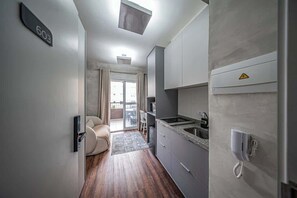 Uma cozinha moderna com fogão embutido, micro-ondas e pia. Há uma porta de correr que dá para uma varanda com vista para a cidade.
