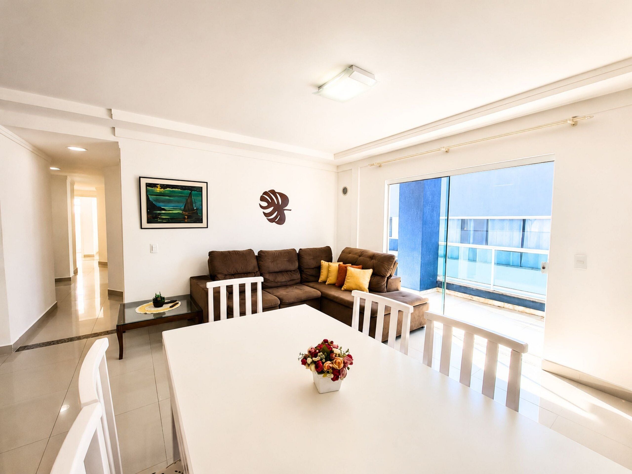 Uma sala de estar moderna com uma mesa de jantar branca, sofá marrom e uma janela ampla com vista.