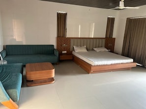 Quarto de hotel moderno com uma cama grande, um sofá, uma mesa de centro de madeira e uma mesa de cabeceira.