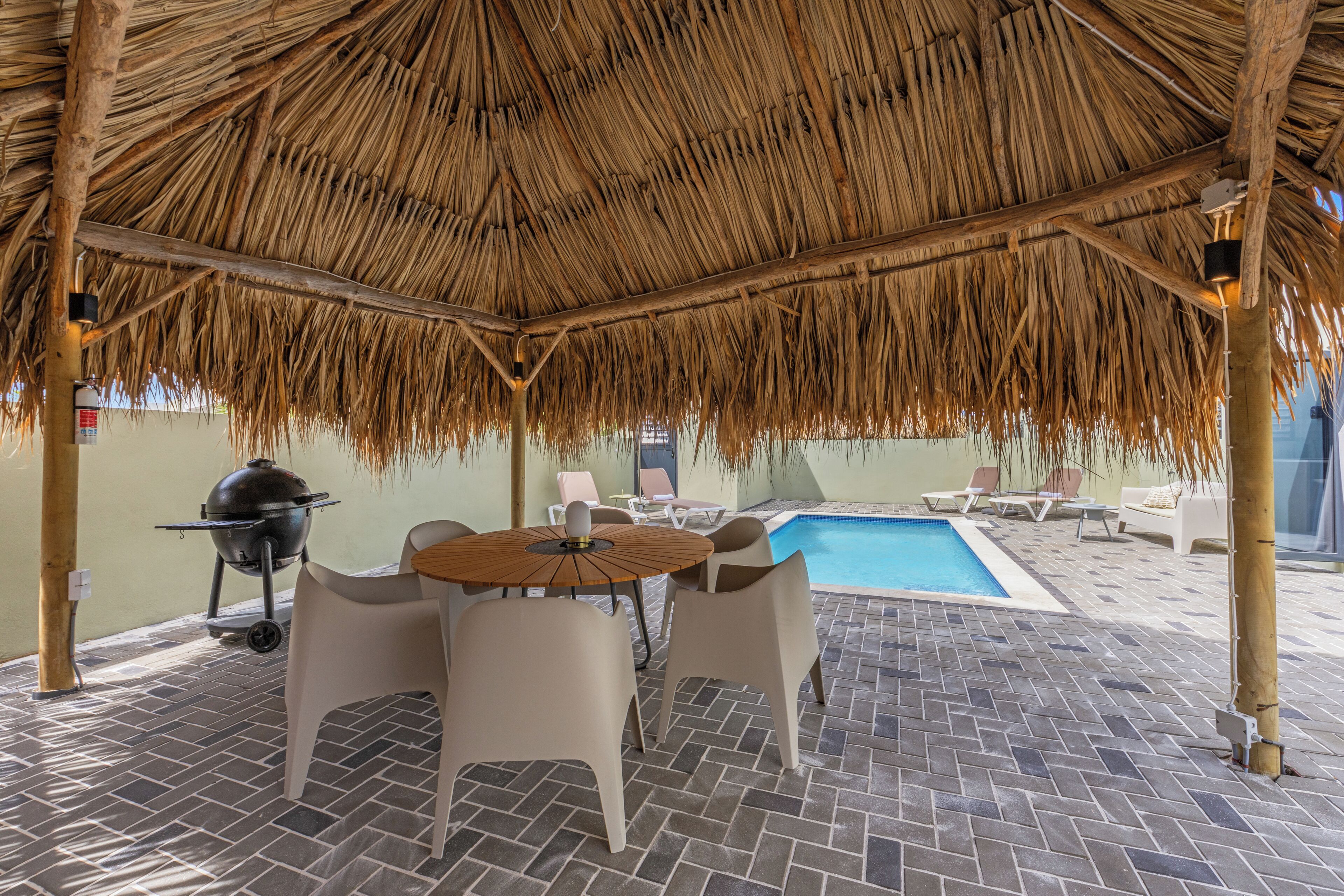 Uma área externa coberta com piscina, espreguiçadeiras e churrasqueira.