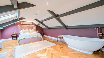 Um quarto com uma cama grande, uma banheira branca e um chão de madeira com padrão herringbone.