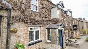 Um edifício de pedra com paredes cobertas de hera, uma placa com o nome Aysgarth Falls Hotel e área de estar ao ar livre.