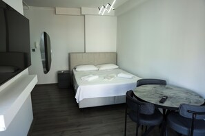 Quarto de hotel com cama, escrivaninha, cadeira, espelho e luminária na parede.