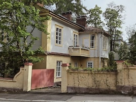 Uma casa de dois andares com varanda, um portão vermelho e uma parede de tijolos.