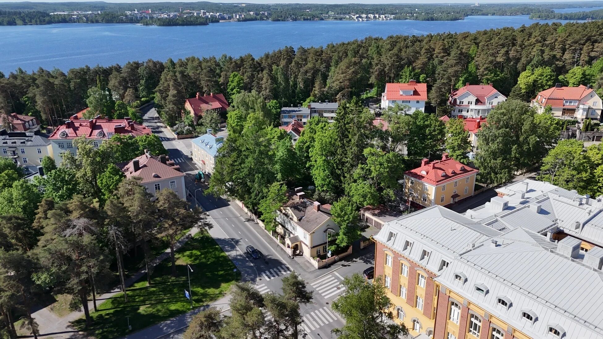 Vista aérea de uma área residencial com casas, uma estrada e um lago ao fundo.