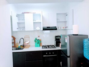 Uma cozinha compacta com armários brancos, fogão a gás, geladeira preta e uma pia pequena.
