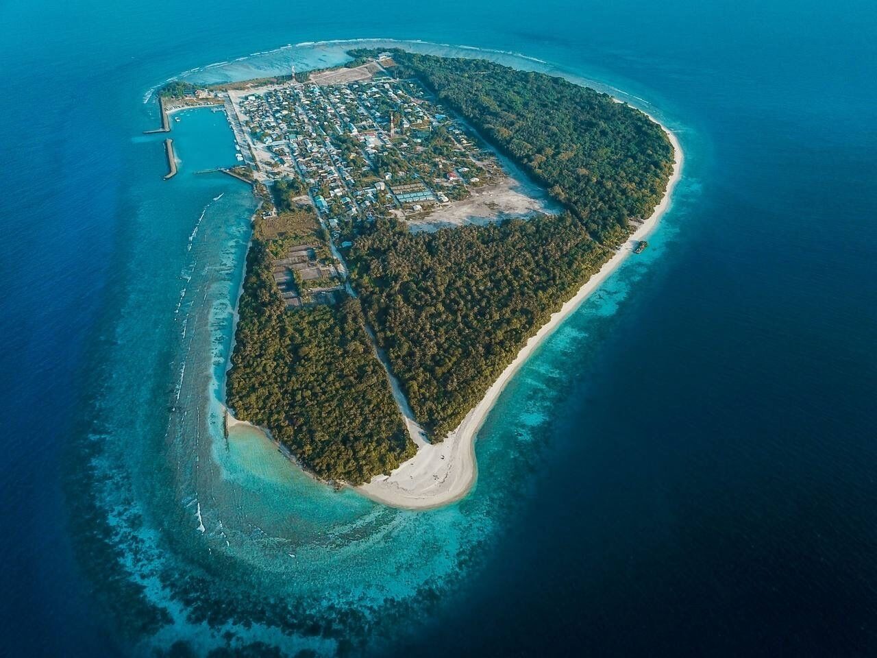 Vista aérea de uma ilha tropical com uma península central, rodeada por águas azul-claras e uma área florestal densa.