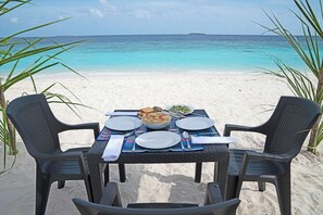 Mesa posta na praia com duas cadeiras, um prato de comida e vista para o oceano.