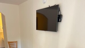 Quarto de hotel com televisão de tela plana fixada na parede, um banco de madeira, micro-ondas e geladeira.