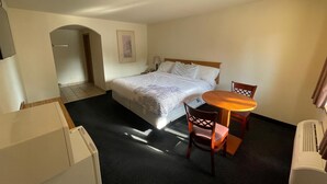 Quarto de hotel com cama, uma mesinha com cadeiras, escrivaninha, poltrona e televisão presa à parede.