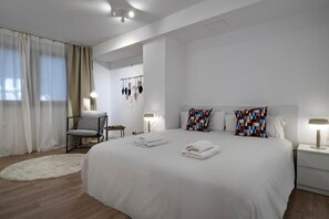 Quarto de hotel moderno com uma cama grande, uma cadeira, uma mesa de cabeceira e um abajur.